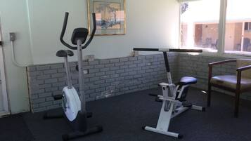 Uma academia com duas bicicletas ergométricas, um quadro na parede e uma janela com vista para o exterior.