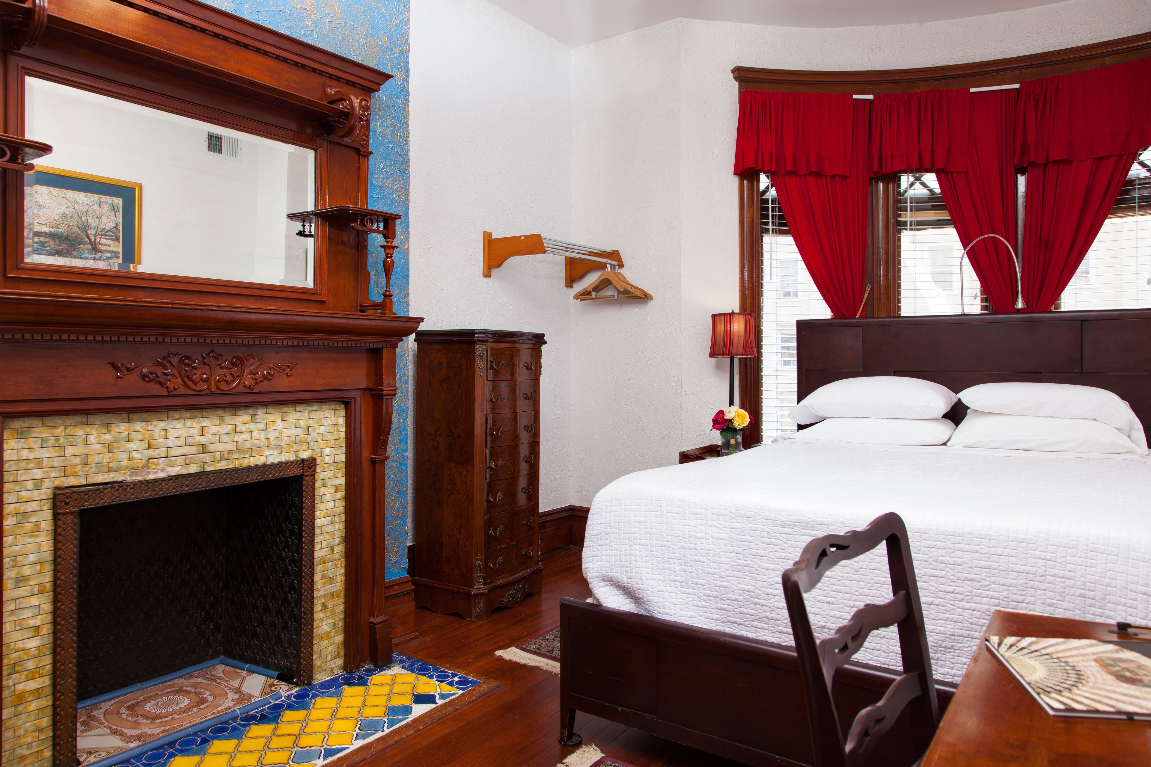 Quarto com cama grande, cómoda de madeira, lareira e espelho.