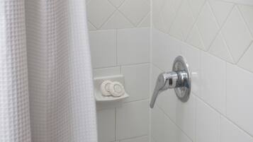 Uma área de chuveiro com chuveiro de metal, um porta-toalhas com uma toalha dobrada e um vaso sanitário com suporte para toalha de papel.
