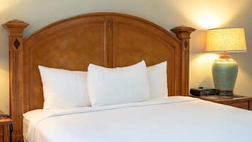 Cama bem arrumada com cabeceira de madeira, luminária de cabeceira e mesa de apoio com um telefone.