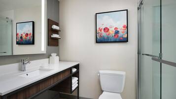 Um banheiro moderno com pia branca, vaso sanitário e box de vidro para o chuveiro. Há duas pinturas florais emolduradas na parede.