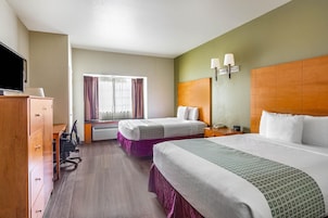 Quarto de hotel com duas camas, uma escrivaninha, uma cadeira, uma televisão e uma janela com cortinas.