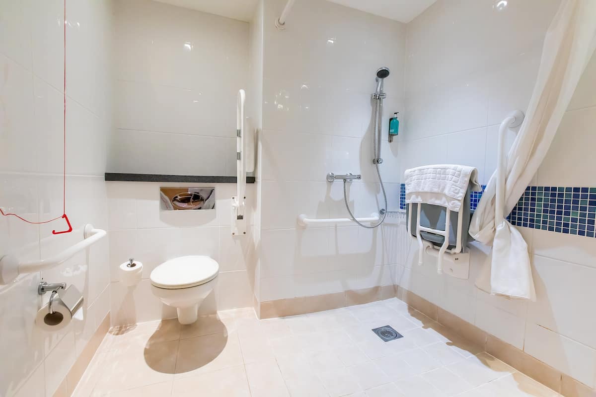 Uma casa de banho moderna com sanita, chuveiro com acessório de duche manual, porta-toalhas e um pequeno armário com produtos de higiene pessoal.