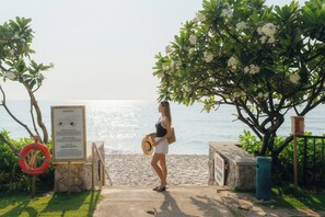 Uma passarela à beira-mar com um boi de salvação, uma placa de aviso e uma árvore com flores brancas.
