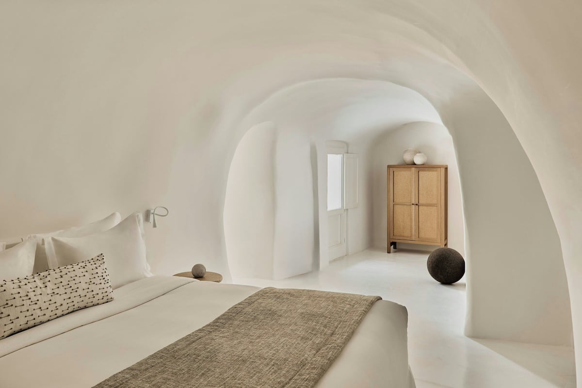 Um quarto minimalista com uma cama, um armário de madeira e uma esfera de pedra.