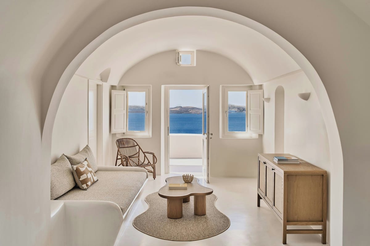 Um quarto aconchegante com teto arredondado, um sofá, uma mesa de centro, um armário e vista para o mar através de portas abertas.