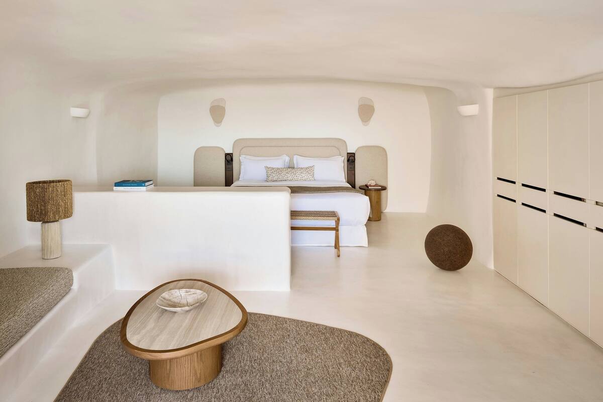 Quarto moderno com cama, mesas de cabeceira, um pequeno espaço de estar e um guarda-roupa.