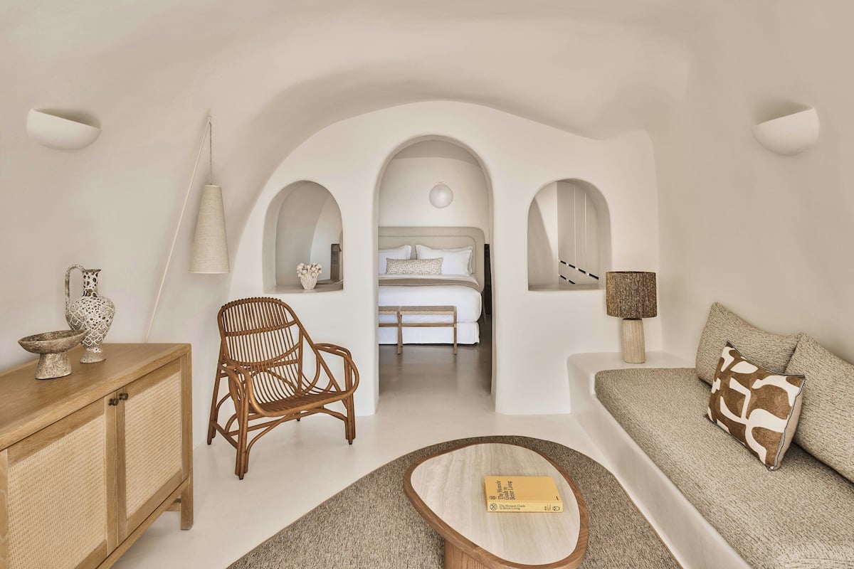 Quarto de hotel moderno com cama, sofá, mesinha de madeira, cadeira de vime e luminária.