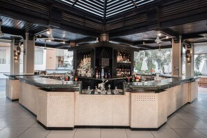 Uma área de bar com uma ilha central e duas divisões, apresentando uma variedade de garrafas e copos.
