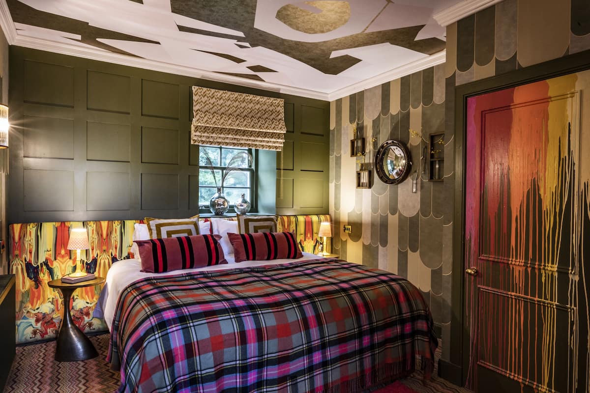 Quarto com uma cama grande, janela com cortinas, espelho fixado na parede e porta com design exclusivo.
