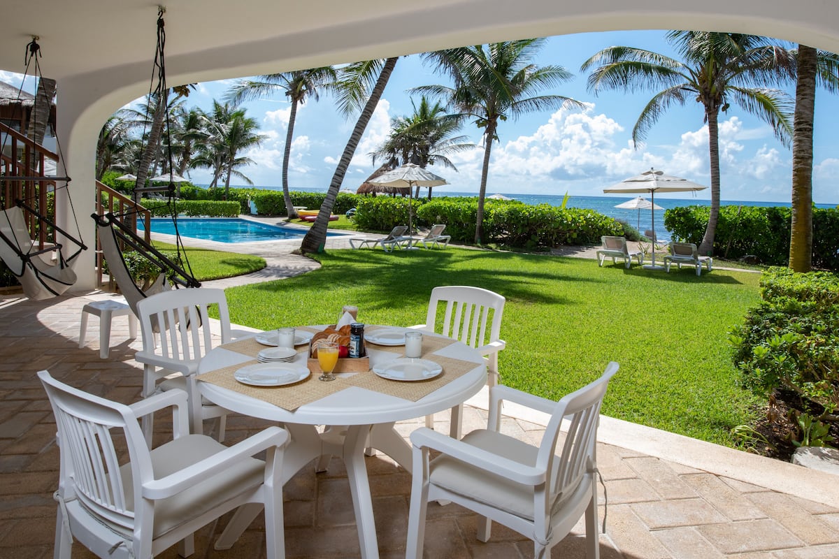 Um pátio com uma mesa posta para quatro pessoas, com vista para uma piscina e palmeiras.