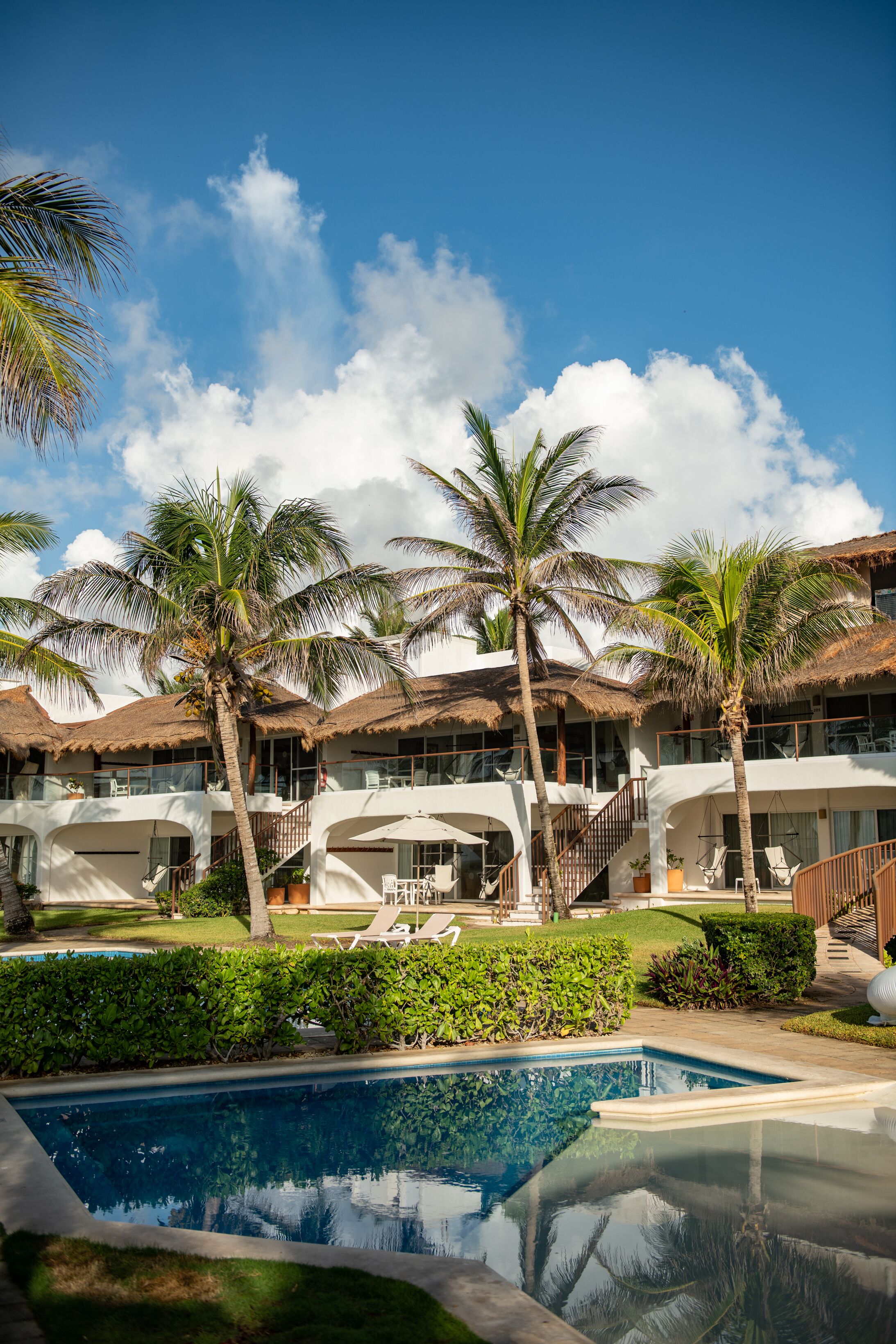Um resort com piscina, palmeiras e um edifício com telhado de palha.