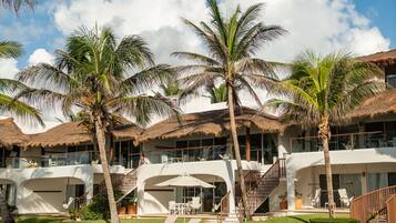 Um resort com piscina, palmeiras e um edifício com telhado de palha.