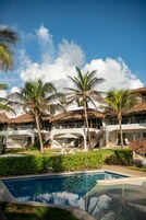 Um resort com piscina, palmeiras e um edifício com telhado de palha.