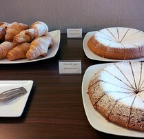 Uma mesa com três pratos de comida: croissants, um bolo e uma torta.