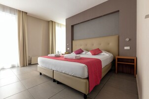 Quarto de hotel com uma cama grande, uma mesinha de cabeceira e vista para o exterior.
