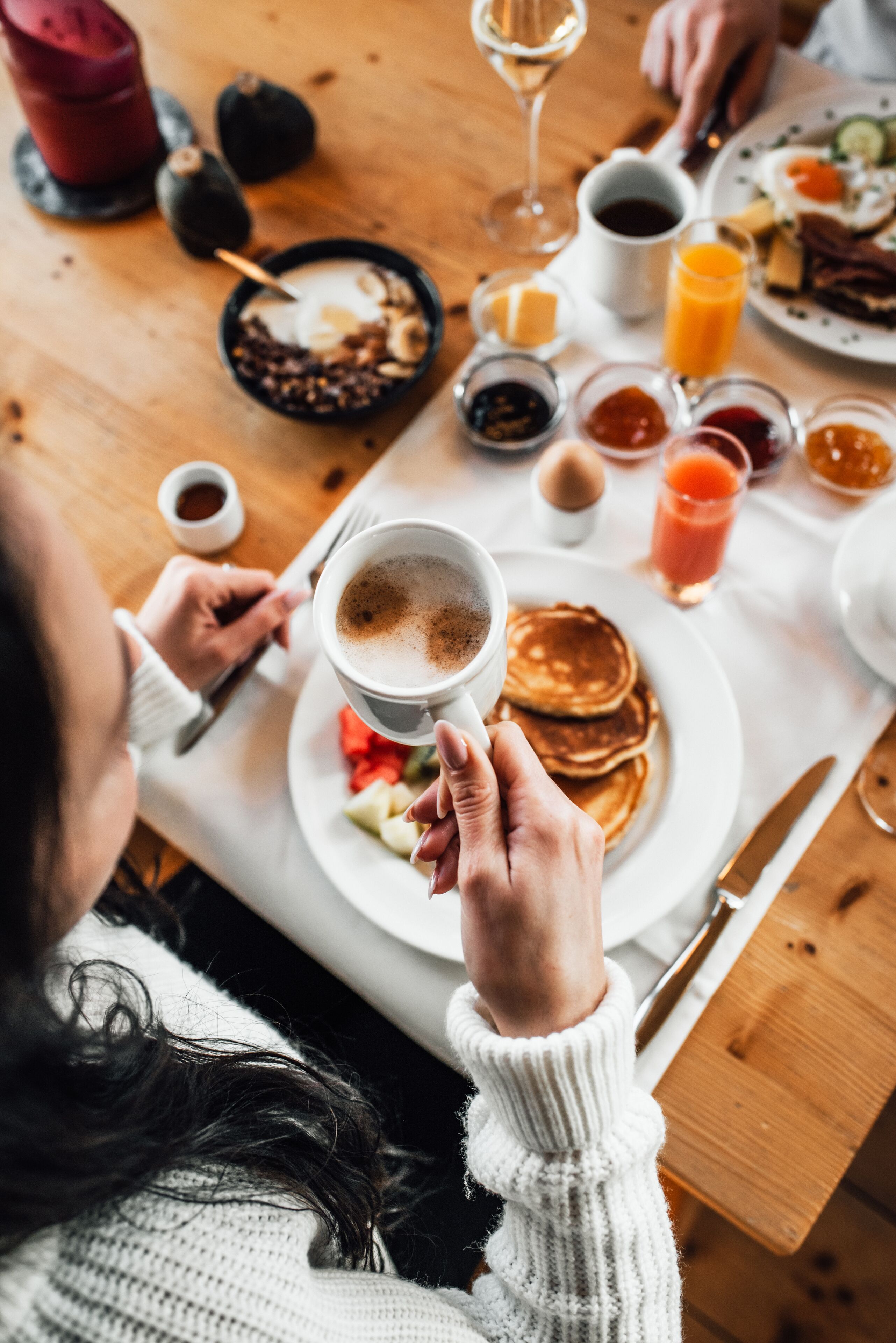 Café da manhã com panquecas, café e diversos acompanhamentos sobre uma mesa de madeira.