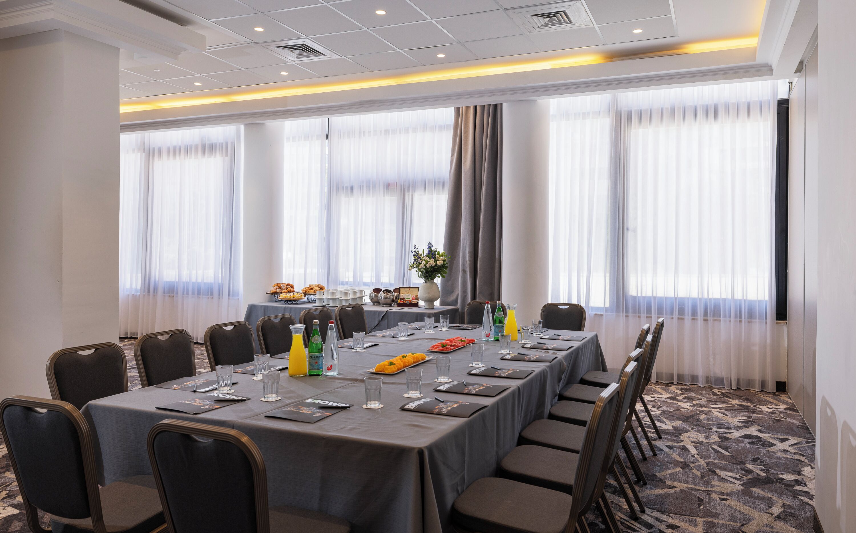 Uma sala de conferências com uma mesa comprida, cadeiras e um buffet com comida e bebidas.