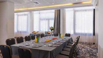 Uma sala de conferências com uma mesa comprida, cadeiras e um buffet com comida e bebidas.