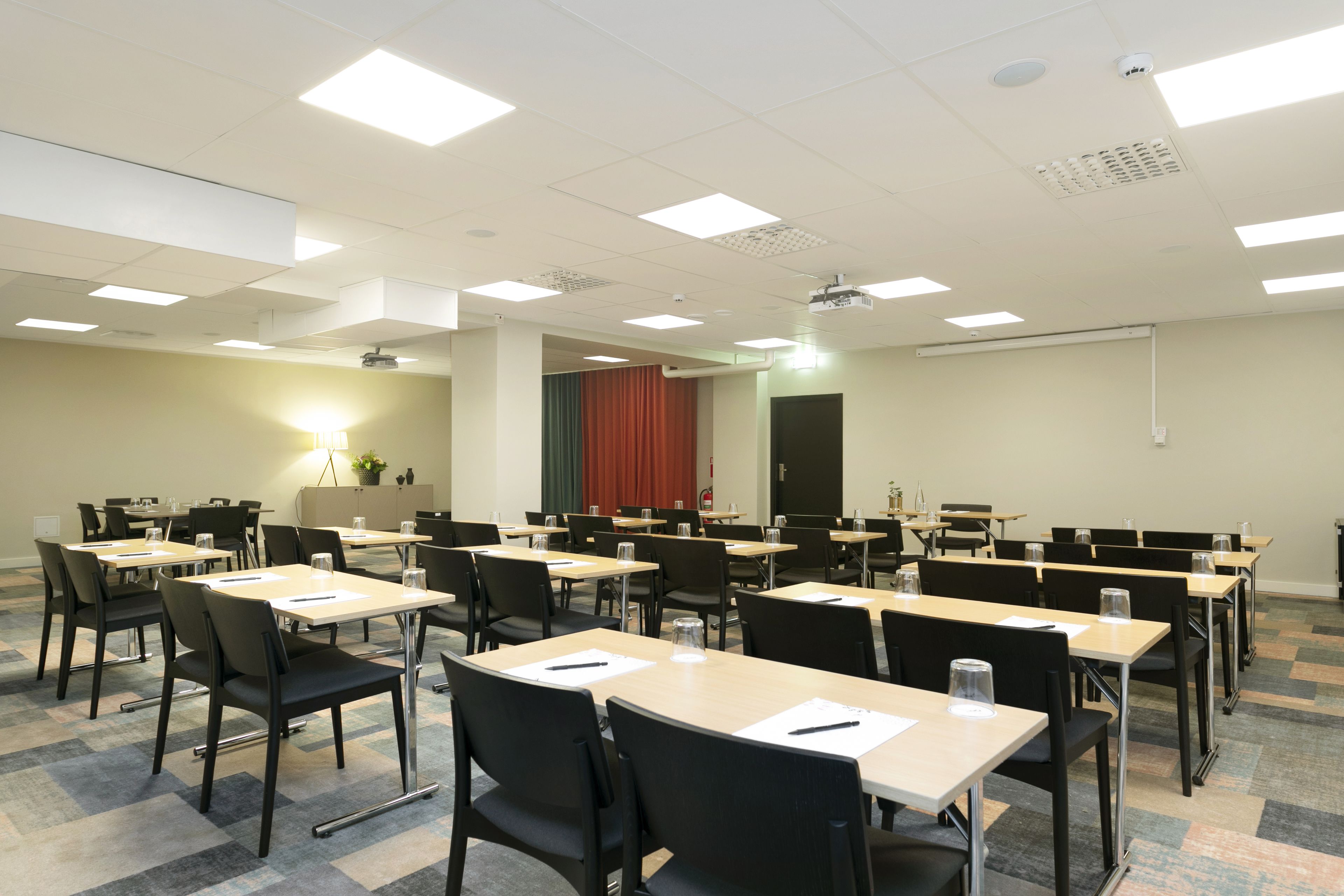 Sala de conferência com várias mesas e cadeiras, equipada com projetores e um palco com cortinas.