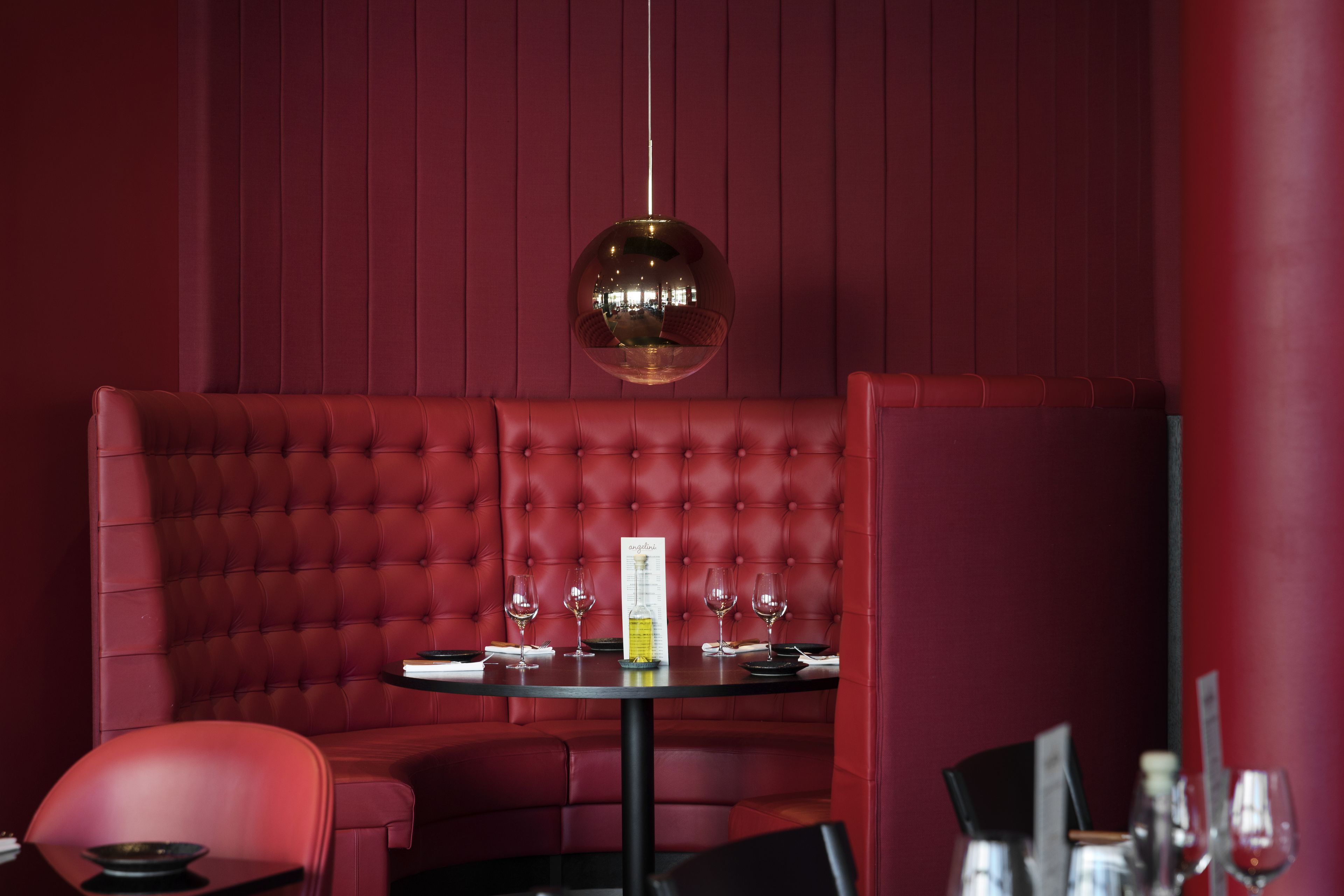 Um estrado vermelho estofado com uma mesa redonda, dois copos de vinho e um menu.