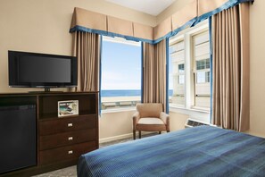 Quarto de hotel com cama, televisão, cadeira e janela com cortinas.