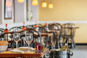 Ambiente de restaurante com mesas preparadas para refeições, incluindo copos de vinho, uma garrafa de vinho e uma cesta de pão.