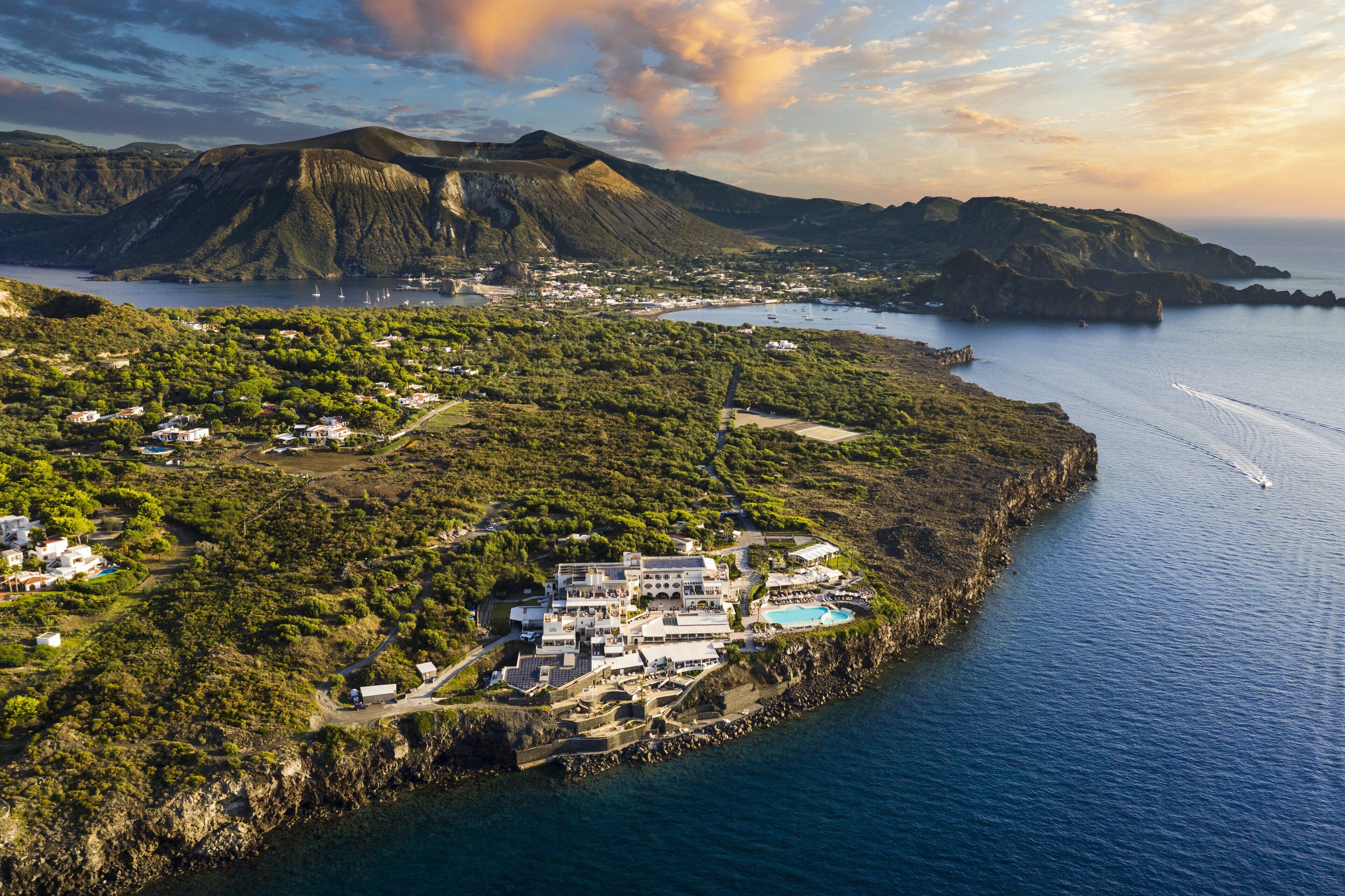 Vista aérea de um resort costeiro com um edifício grande, piscina e um porto de iates.