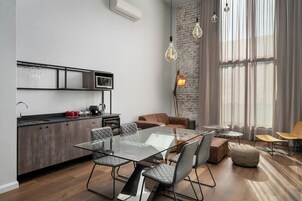 Cozinha moderna com área de jantar, destacando uma mesa de vidro, armários escuros e uma parede com detalhes em tijolo.