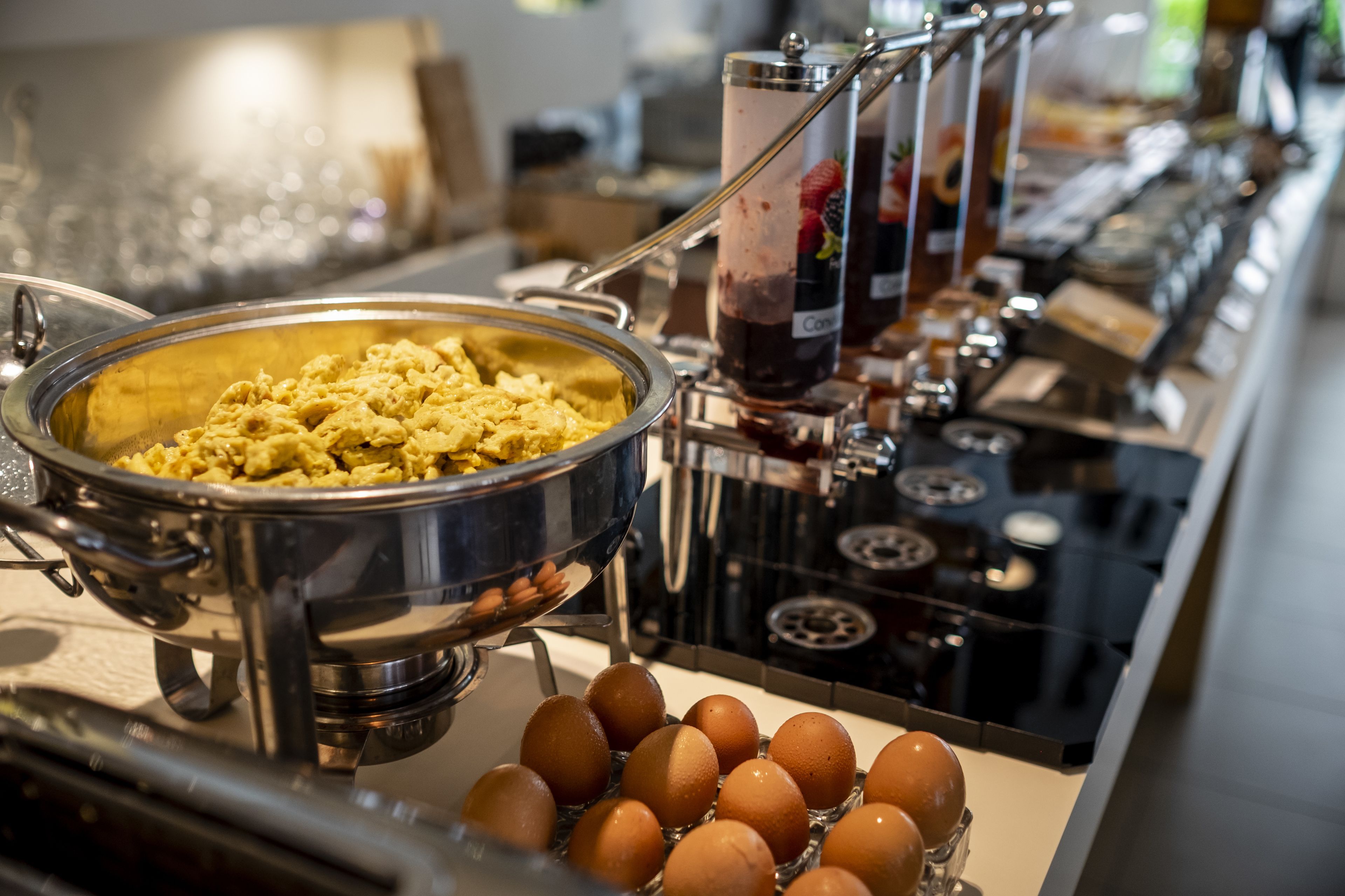 Buffet com uma grande panela de ovos mexidos, um recipiente com ovos e uma máquina de café.