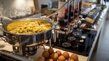 Buffet com uma grande panela de ovos mexidos, um recipiente com ovos e uma máquina de café.