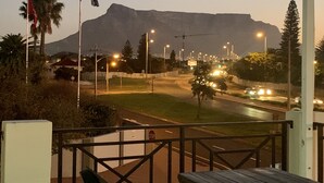 Vista de uma estrada com uma montanha ao fundo, postes de luz e palmeiras.