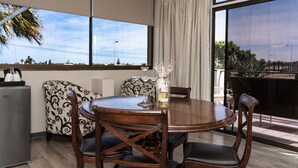 Uma área de refeições com mesa e cadeiras de madeira, um sofá estampado e um minibar.
