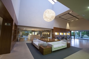 Um hall espaçoso com teto alto, um grande balcão de recepção em madeira e áreas de estar.