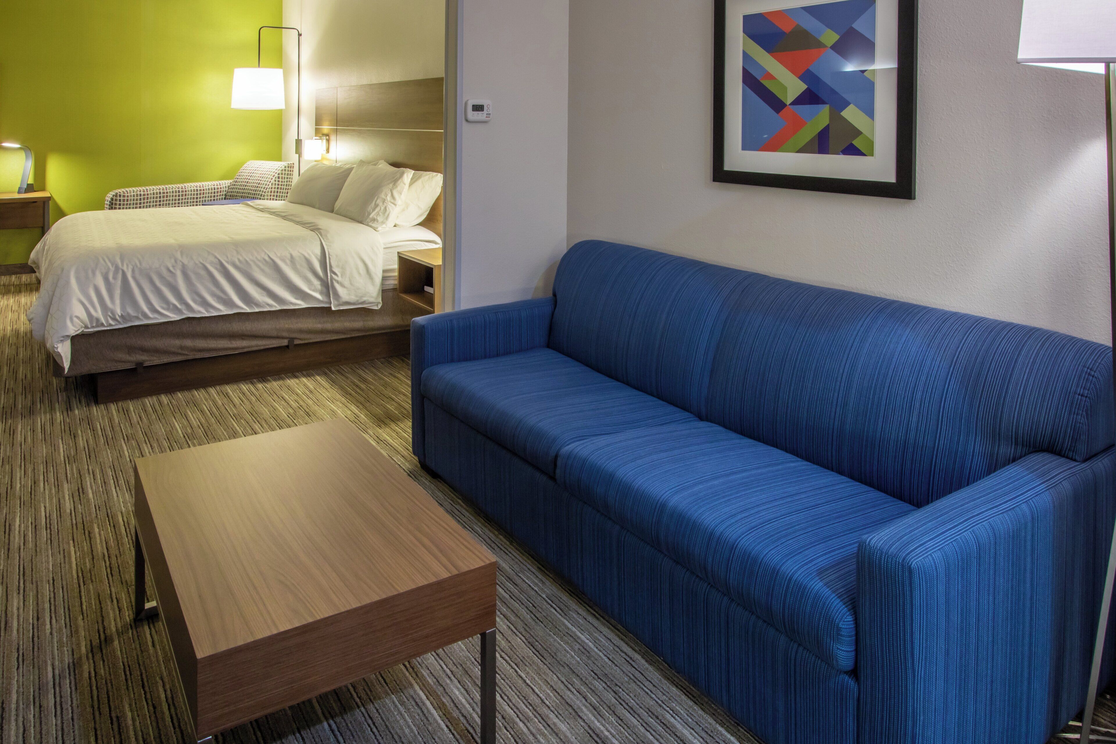 Quarto de hotel com cama, sofá azul, mesa de madeira e um quadro na parede.