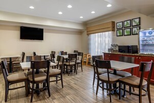 Uma sala de jantar com várias mesas e cadeiras, uma televisão de tela plana na parede e um frigorífico com congelador.