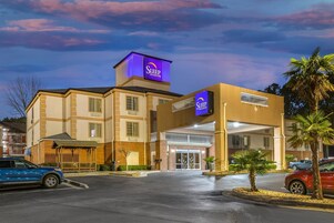 Um hotel com um letreiro grande que diz "Sleep Inn & Suites", uma entrada coberta e uma área de estacionamento com carros.