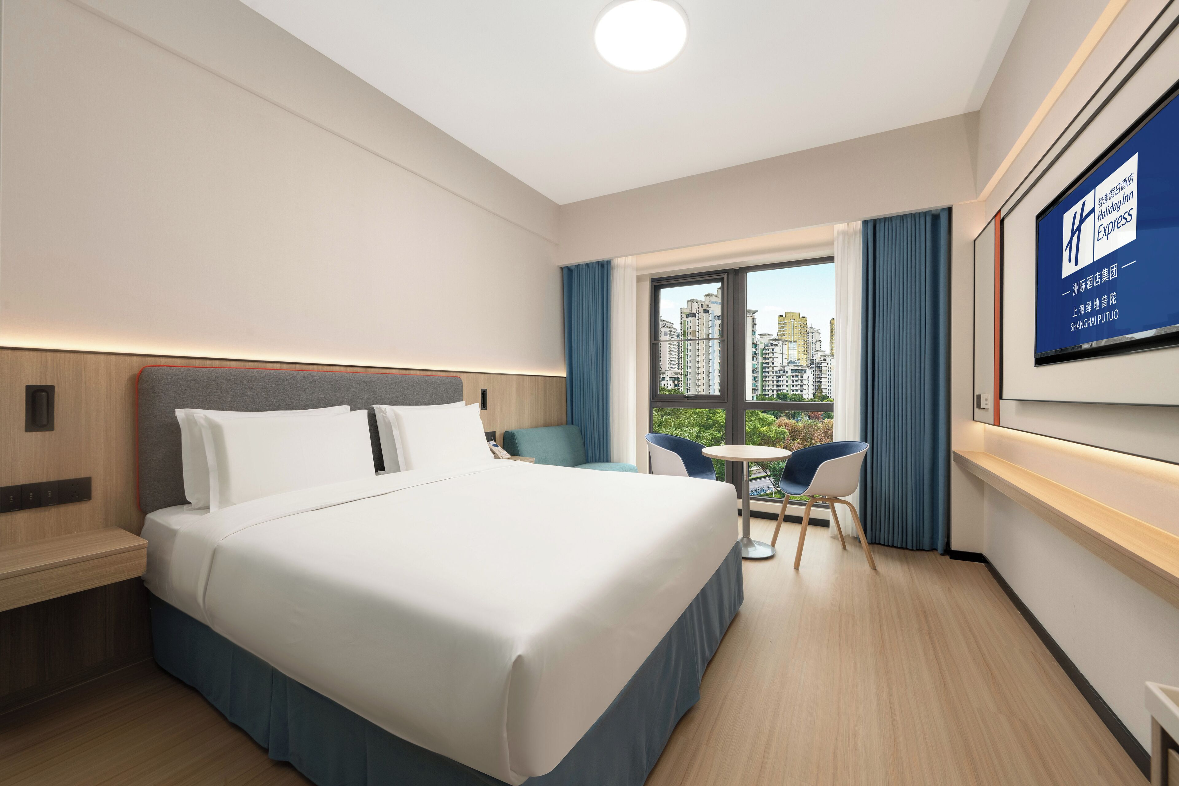 Quarto de hotel com uma cama grande, uma mesa, uma cadeira e uma televisão na parede.