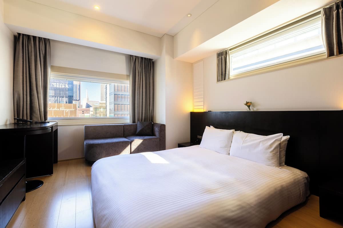 Quarto de hotel com uma cama grande, uma escrivaninha, uma cadeira e uma janela com cortinas.