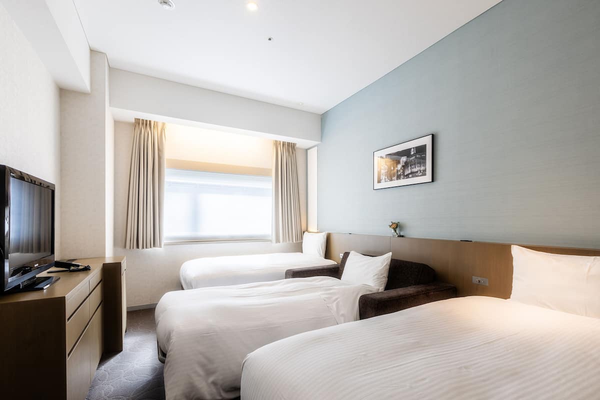 Quarto de hotel com duas camas, uma televisão e uma janela com cortinas.
