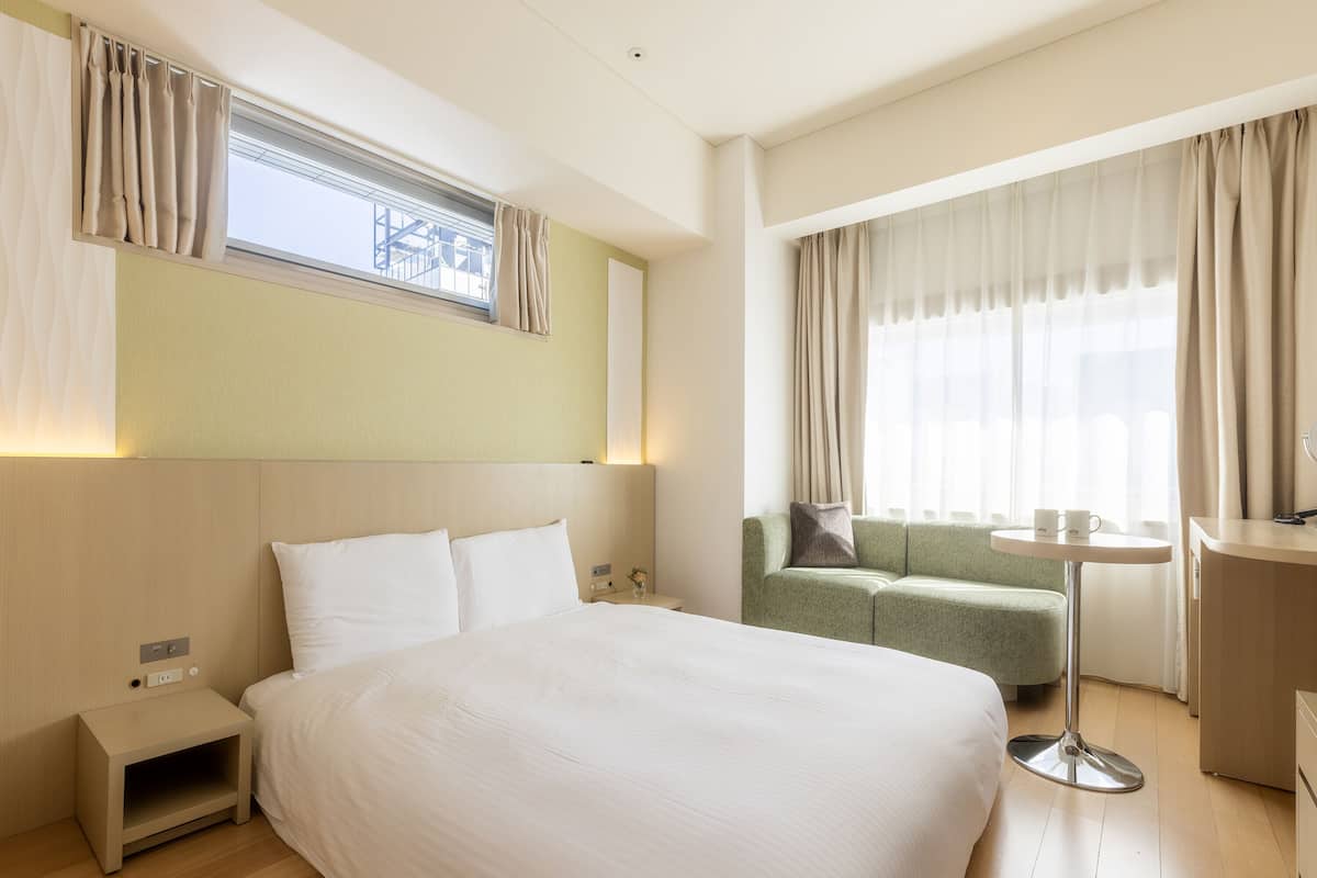 Quarto de hotel com uma cama grande, um sofá pequeno, uma mesa redonda e uma janela com cortinas.