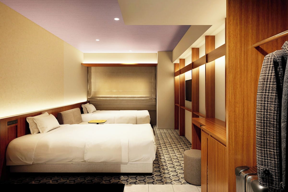 Quarto de hotel com uma cama grande, mesa de cabeceira, guarda-roupa e mala.