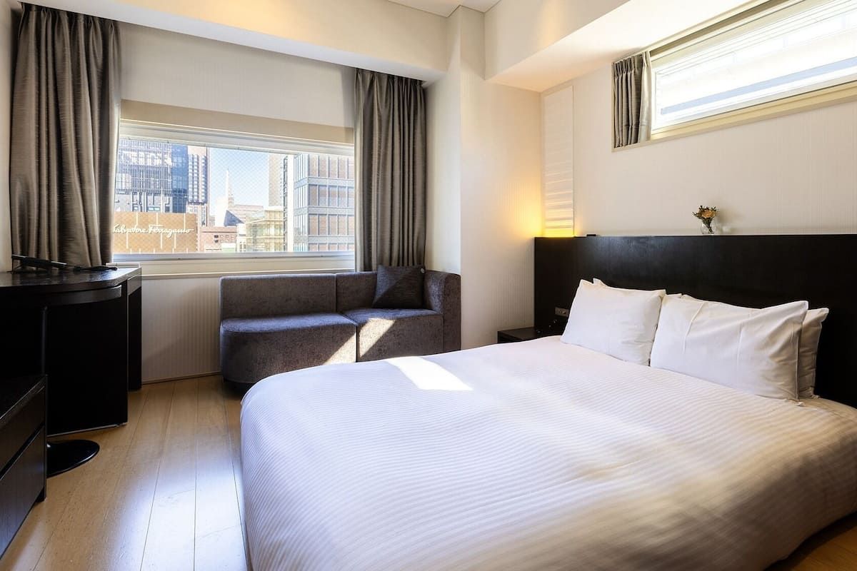 Quarto de hotel com uma cama grande, um sofá, uma escrivaninha e uma janela com cortinas.