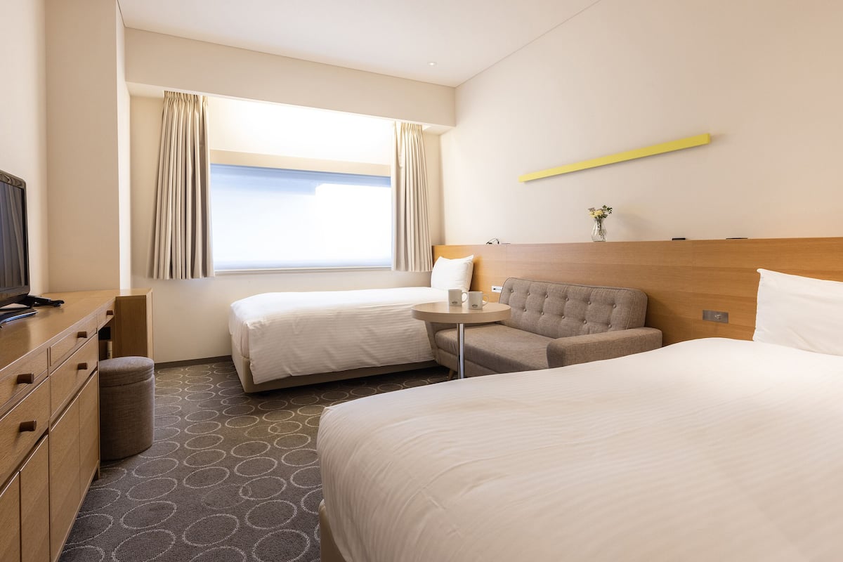 Quarto de hotel com duas camas, um sofá, uma mesa redonda pequena e uma televisão.