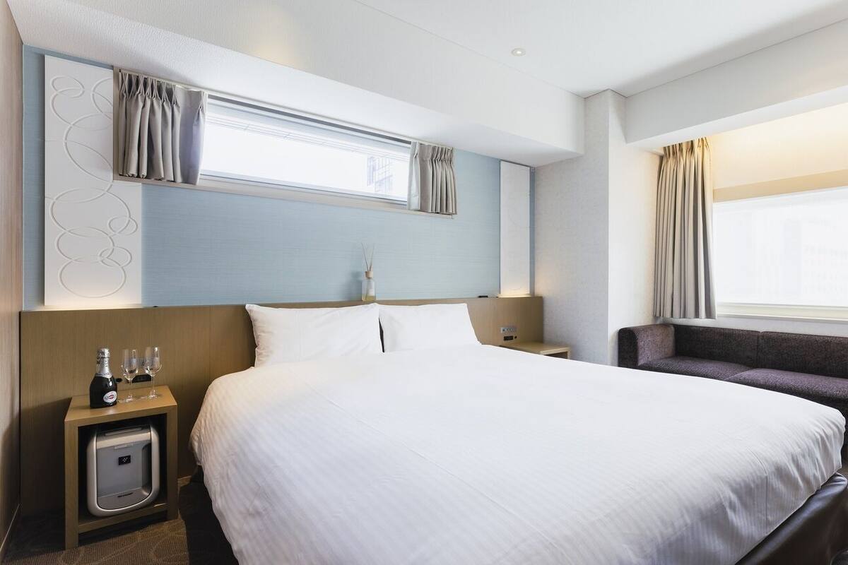 Quarto de hotel com cama grande, área de estar, minibar e janela com cortinas.
