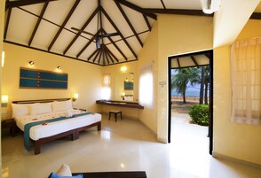 Quarto de hotel com uma cama grande, uma escrivaninha, um espelho e vista para a praia.