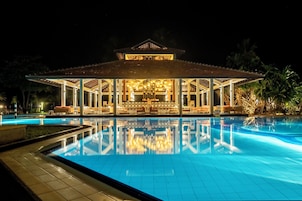 Vista noturna de um hotel com piscina, área de estar coberta ao ar livre e estilo arquitetônico tradicional.