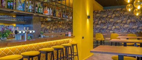 Uma área de bar com banquetas, balcão e estantes com garrafas.