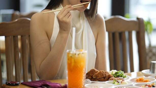 Uma pessoa sentada à mesa de madeira com diversos pratos, uma bebida e pauzinhos.
