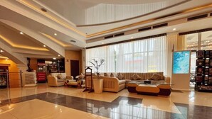 Um hall amplo com área de estar espaçosa, balcão de recepção e uma grande janela com cortinas.